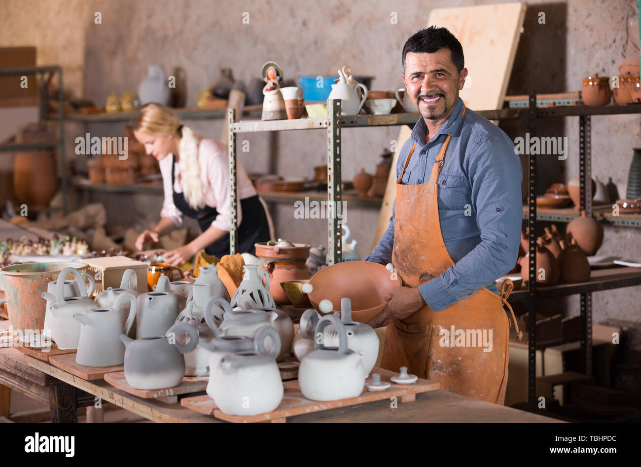 happy russian man and woman potters holding ceramic vessels in atelier ...