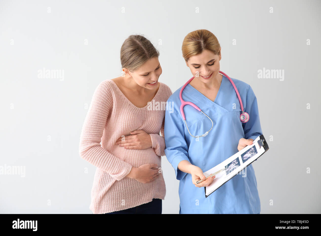 Gynecologist with young pregnant woman on light background Stock Photo ...