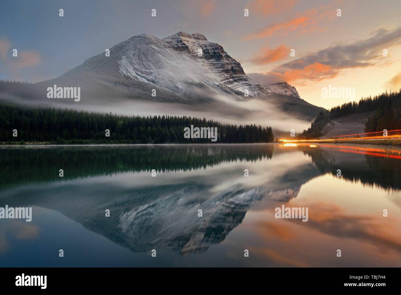Mountain lake and traffic light trail with reflection and fog at sunset ...