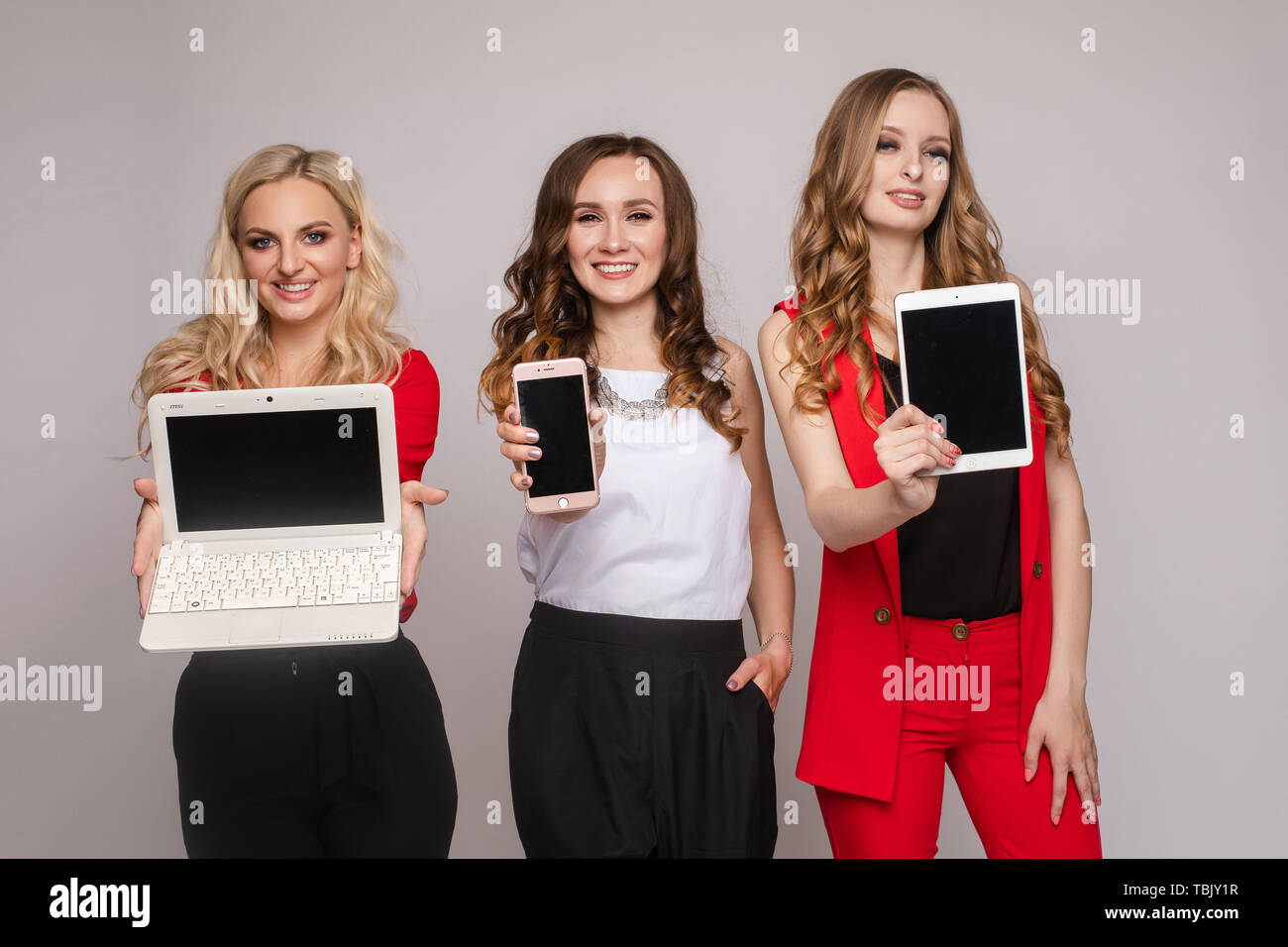 Three ladies using gadgets. Three gorgeous elegant young women in ...