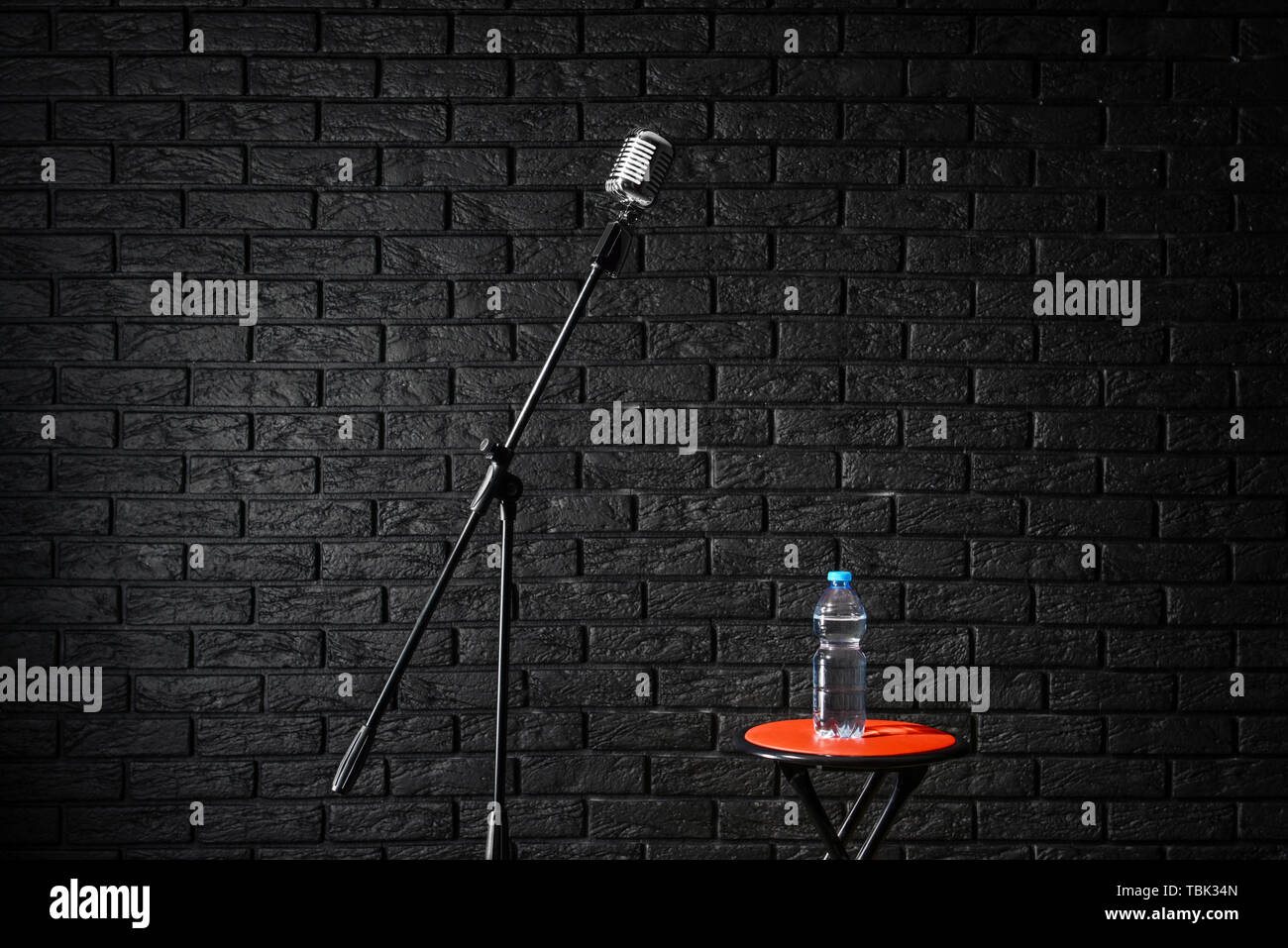 Microphone with stool and bottle of water on dark brick background ...