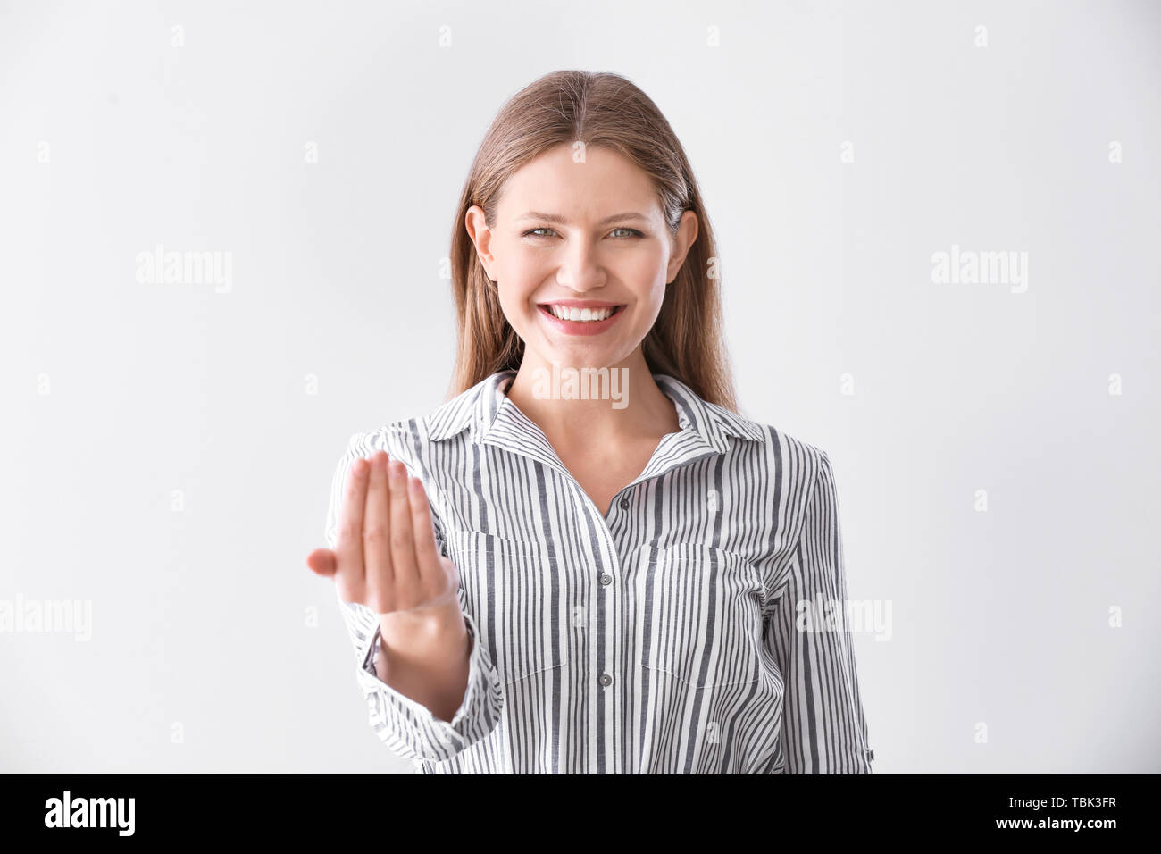 Beautiful young woman inviting viewer against light background Stock ...