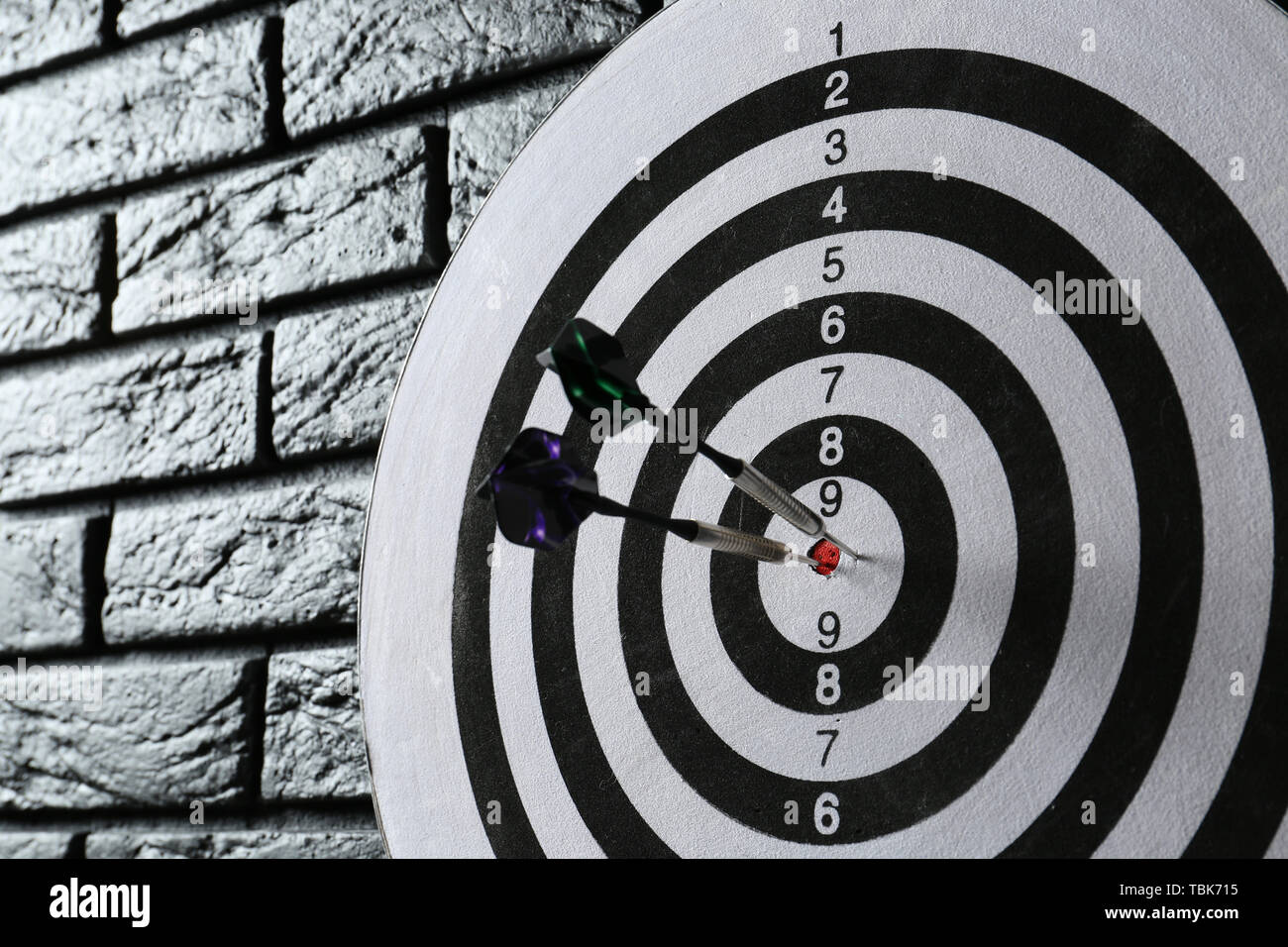 Dartboard with hit bullseye on dark brick wall, closeup Stock Photo - Alamy