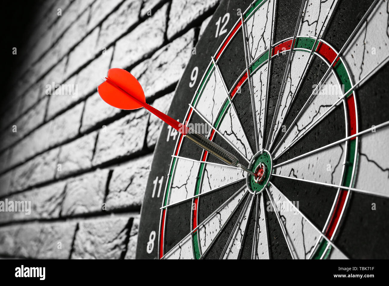 Dartboard with hit bullseye on dark brick wall, closeup Stock Photo - Alamy