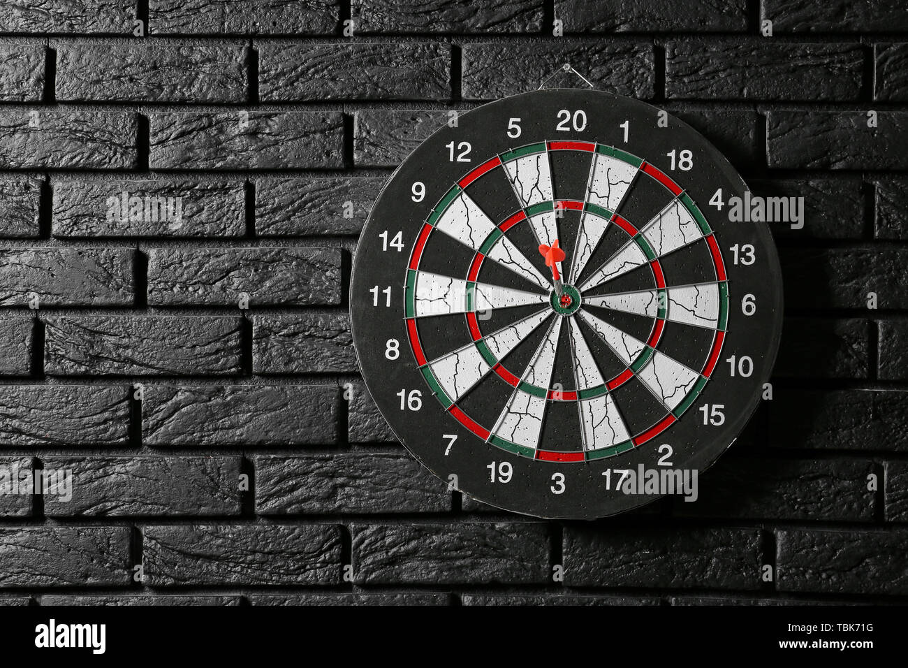 Dartboard with hit bullseye on dark brick wall Stock Photo - Alamy