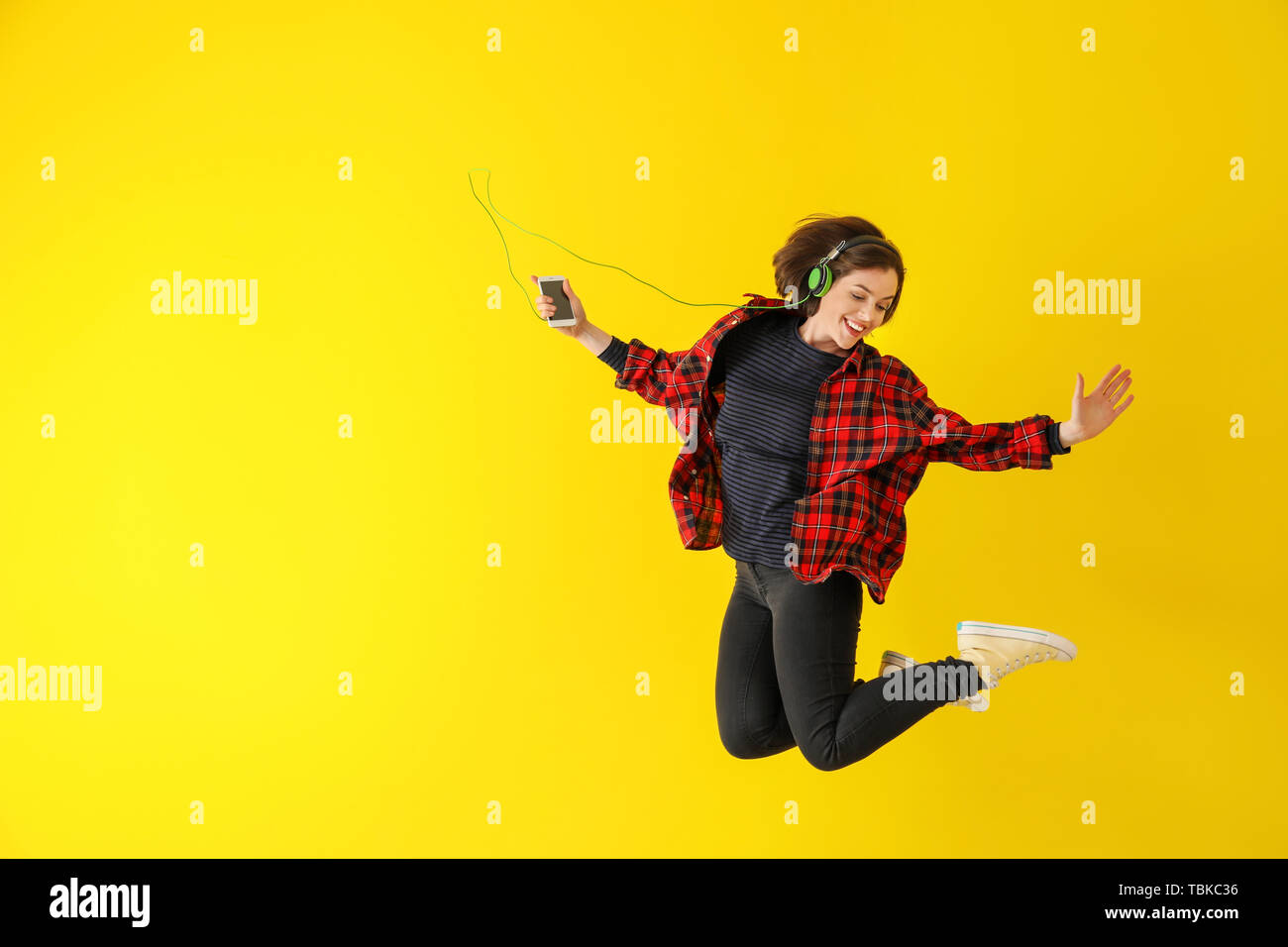 Jumping young woman with with headphones and mobile phone against color ...