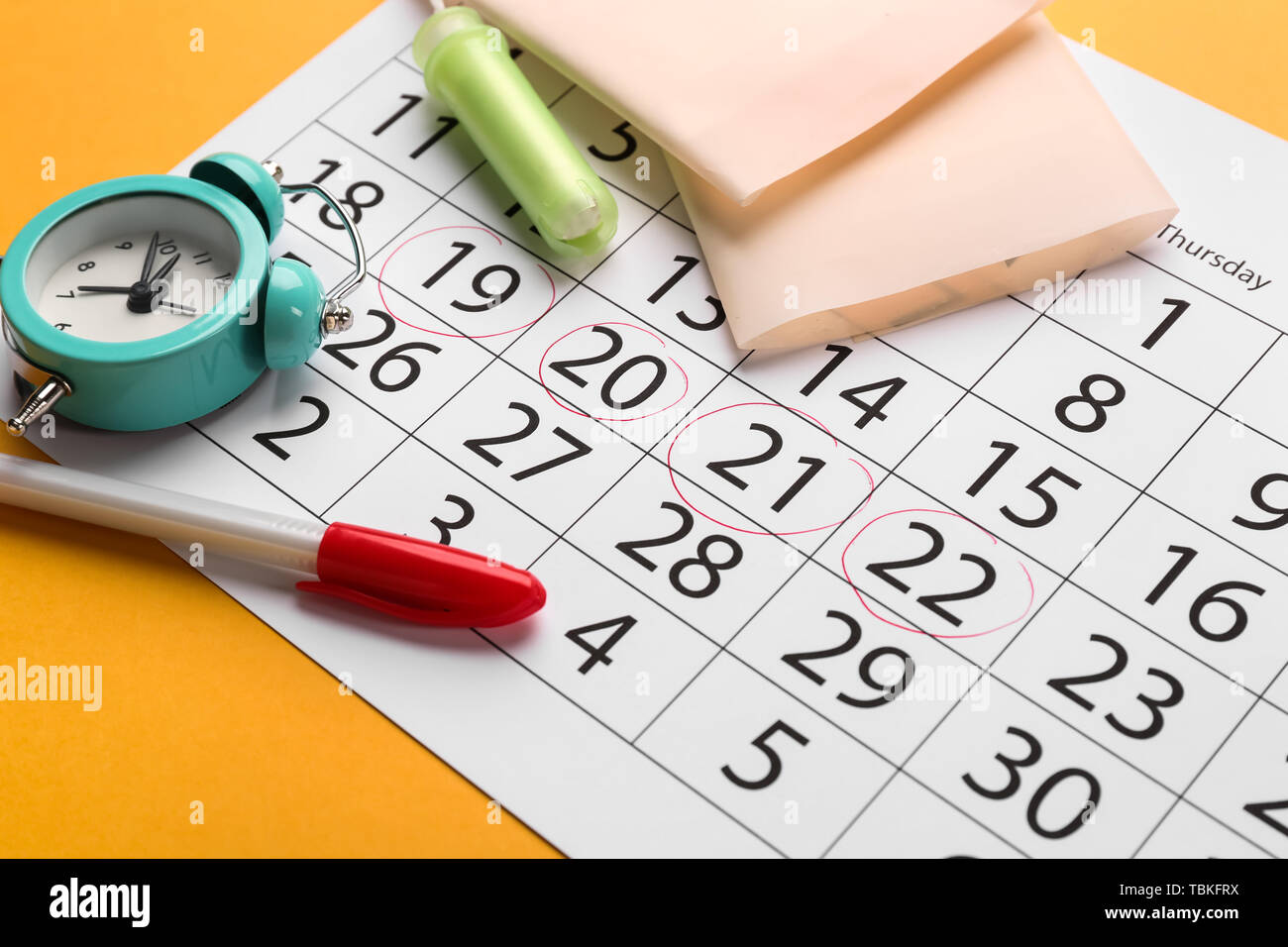 Menstrual calendar with feminine products and alarm clock on color ...