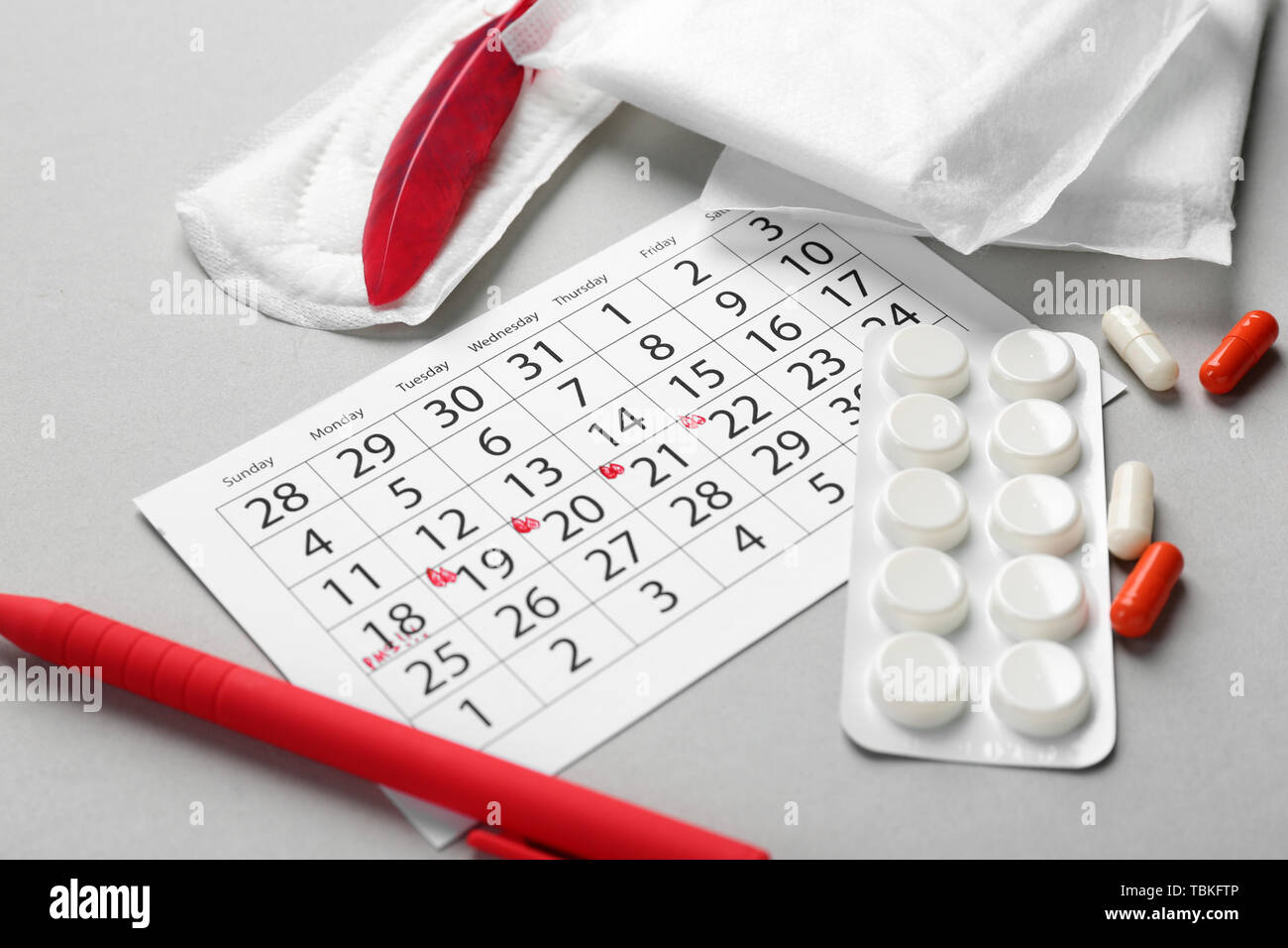 Menstrual calendar with feminine products and pills on grey background ...