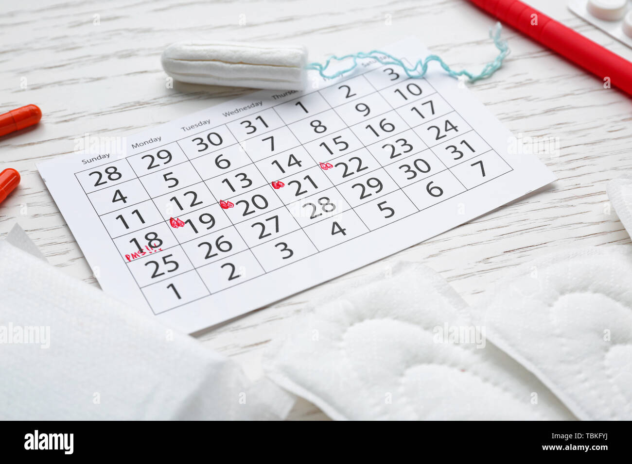 Menstrual calendar with feminine products and pills on white table ...