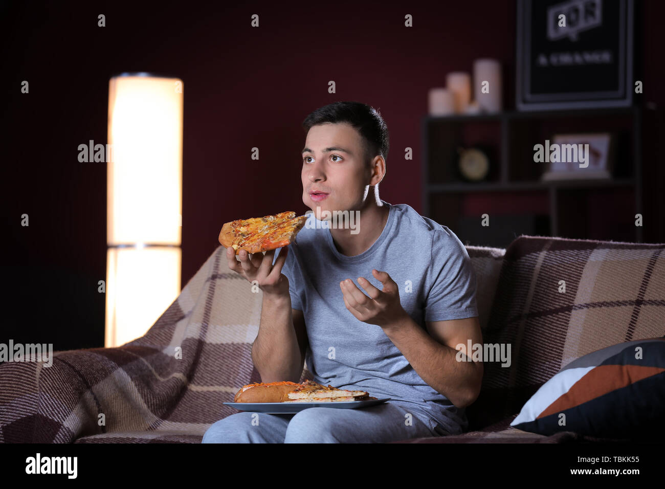 Handsome young man eating unhealthy food while watching TV at night ...