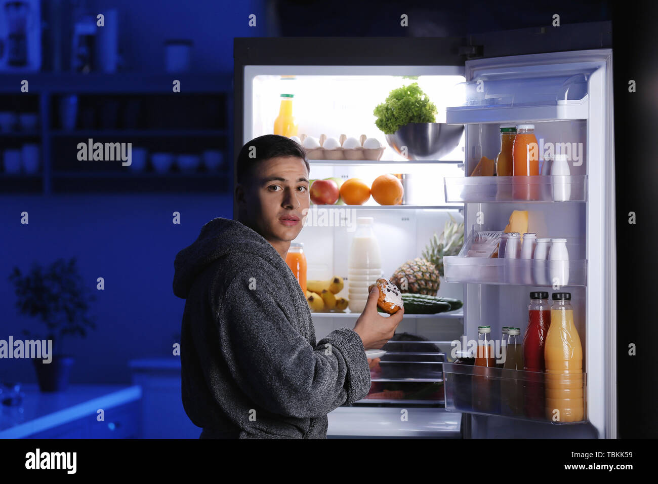 Afraid man caught in the act of eating unhealthy food near refrigerator ...
