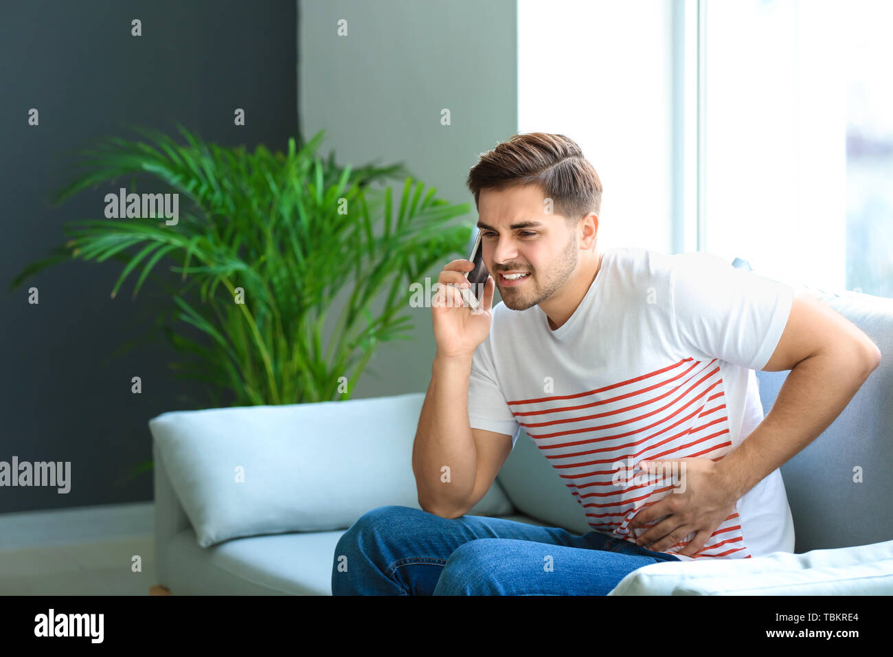 Young man calling an ambulance while suffering from abdominal pain at ...