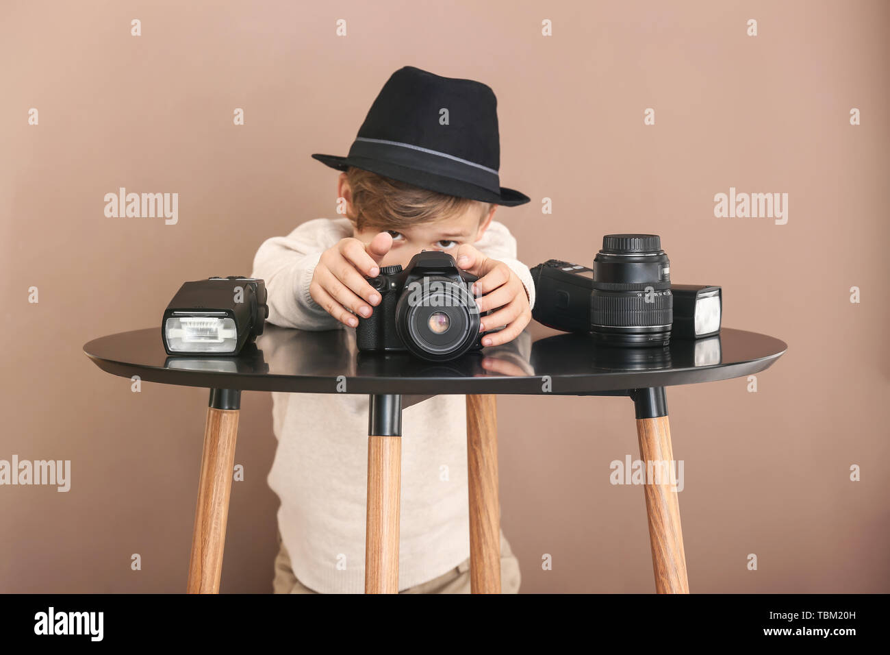 Cute little photographer with professional camera on color background ...