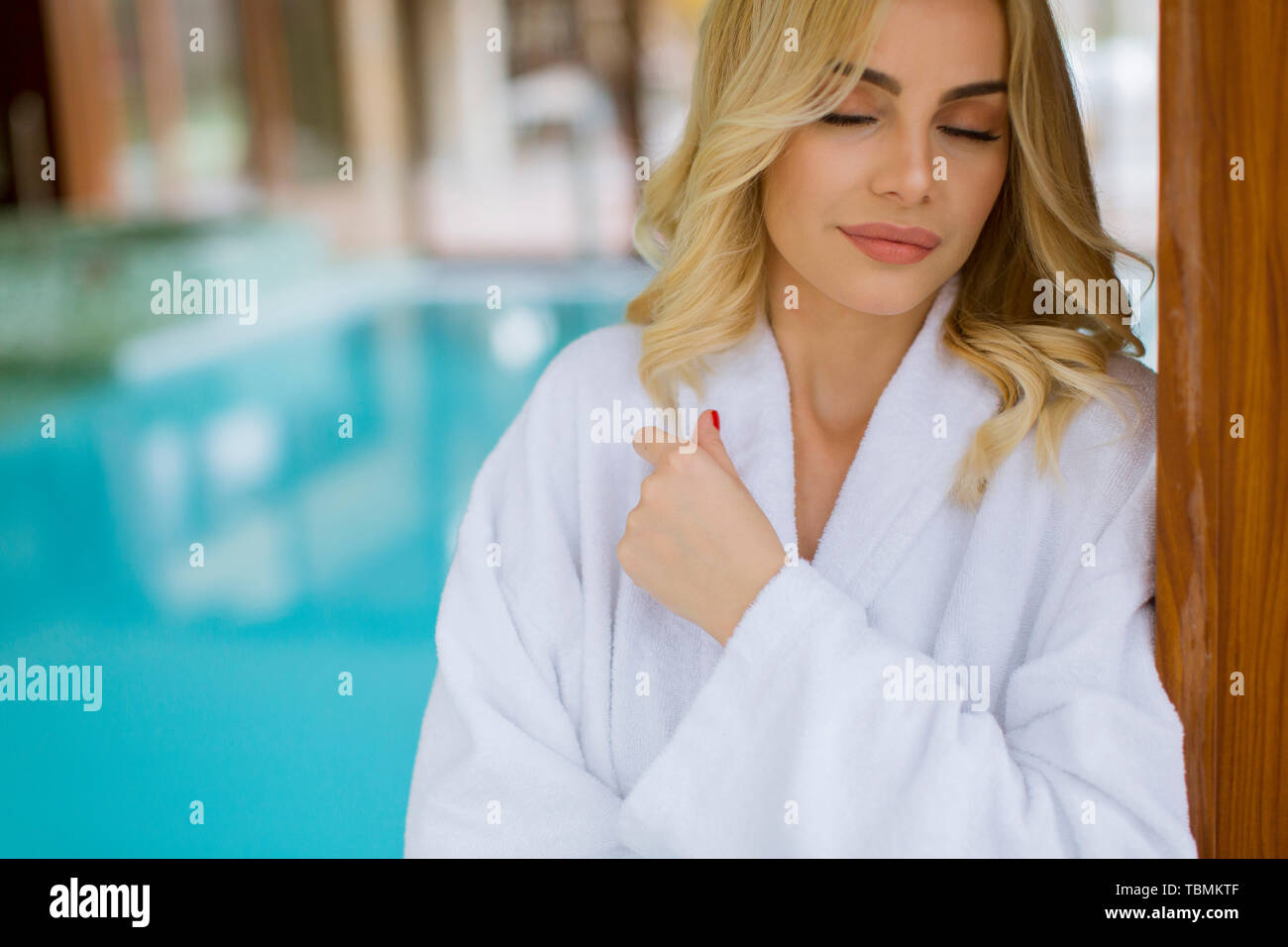 Beautiful young blonde woman in bathrobe relaxing at indoor swimming ...