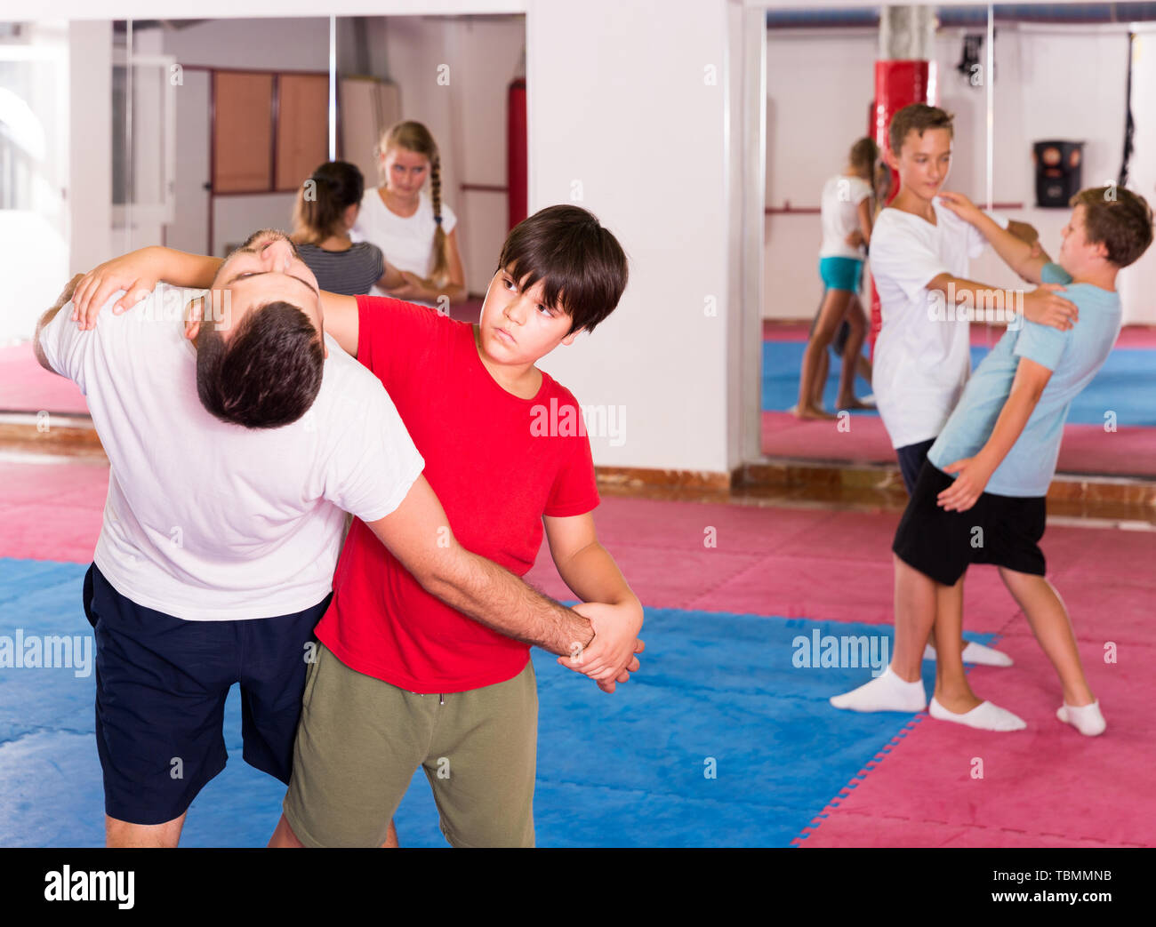 Adult and teen people practicing self defence technique in pairs at gym ...