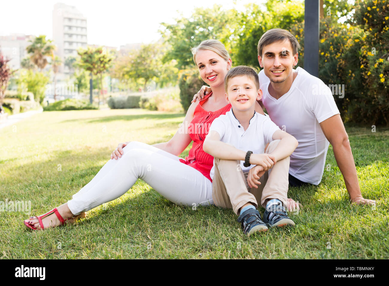 young happy russian parent with boy in teen age sitting on green grass ...