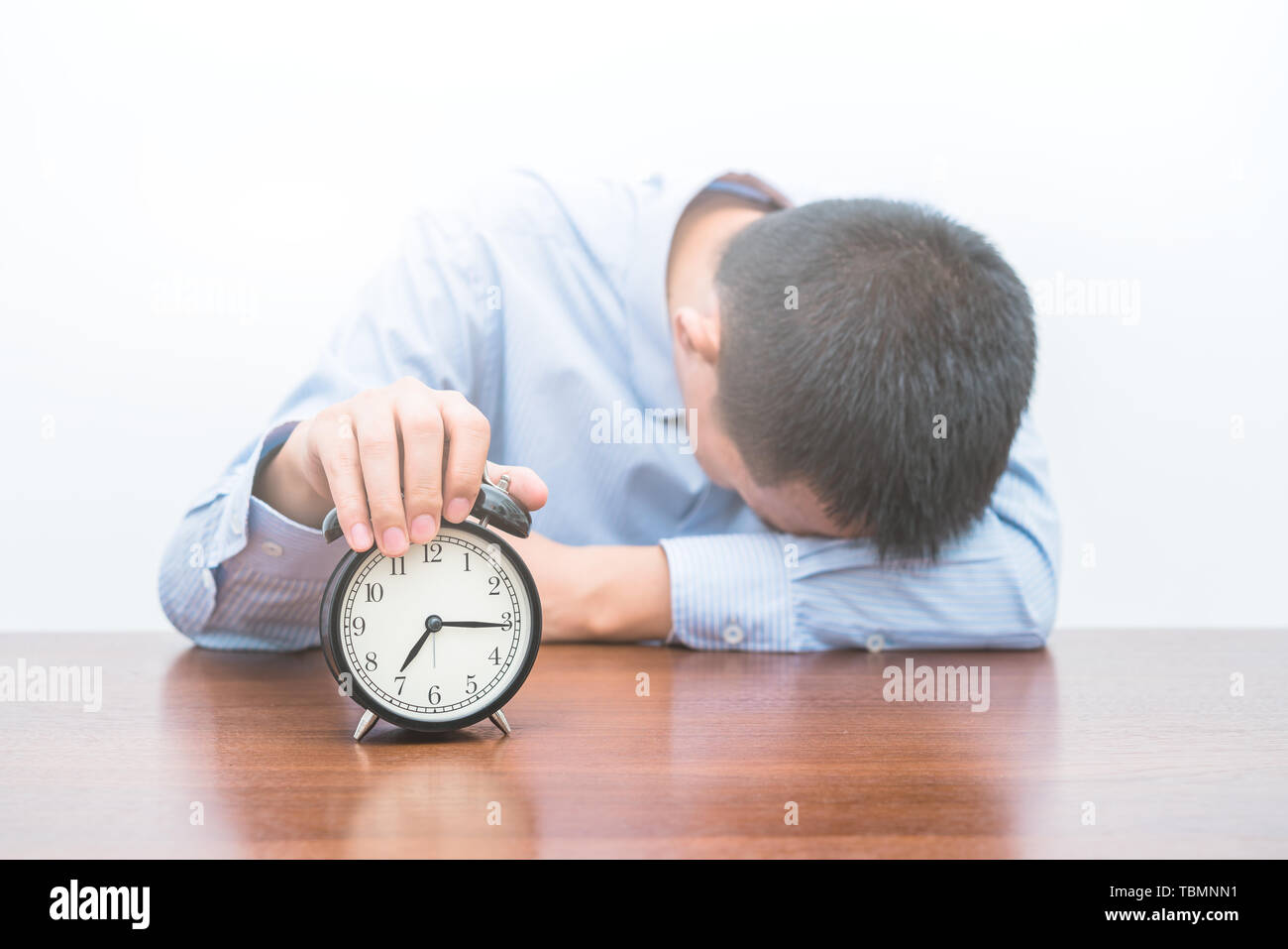 A tired young man holds the alarm clock Stock Photo - Alamy