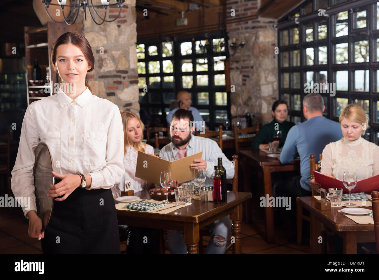 Attractive young waitress with serving tray welcoming in cosy ...