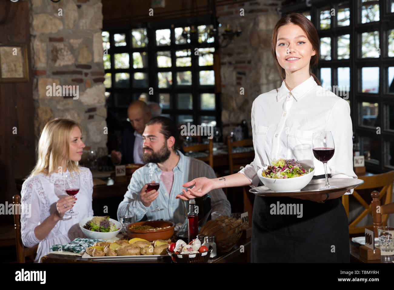 Attractive young waitress with serving tray welcoming in cosy ...