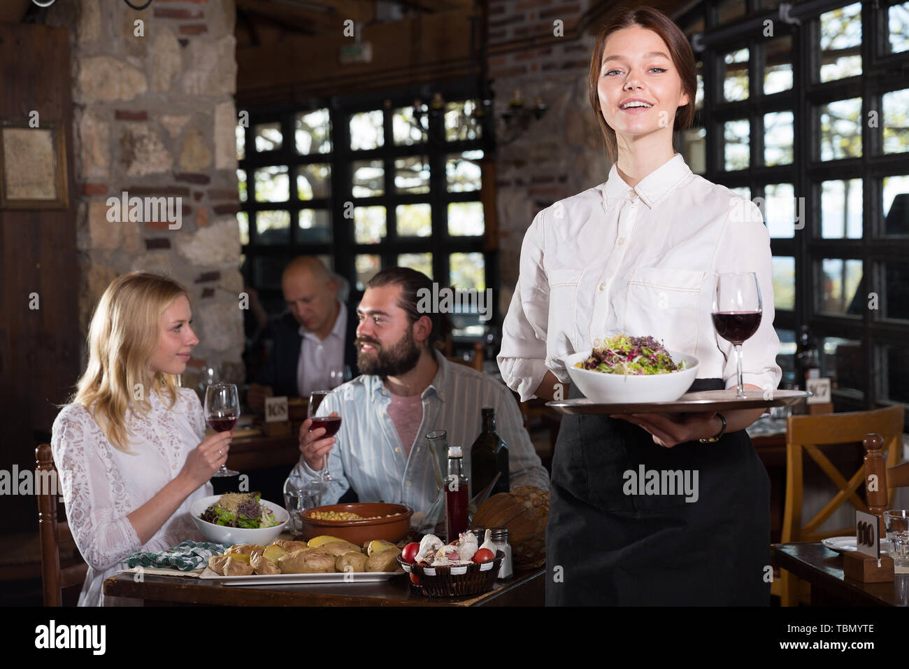 Professional waitress greeting customers at table in rustic restaurant ...