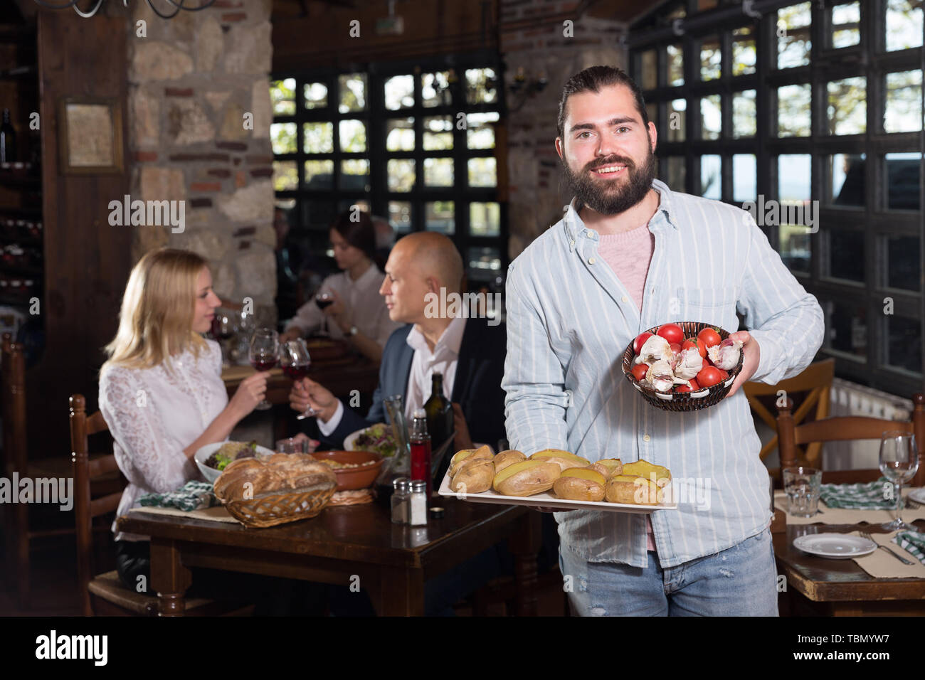 Positive male waiter welcoming guests to country restaurant Stock Photo ...