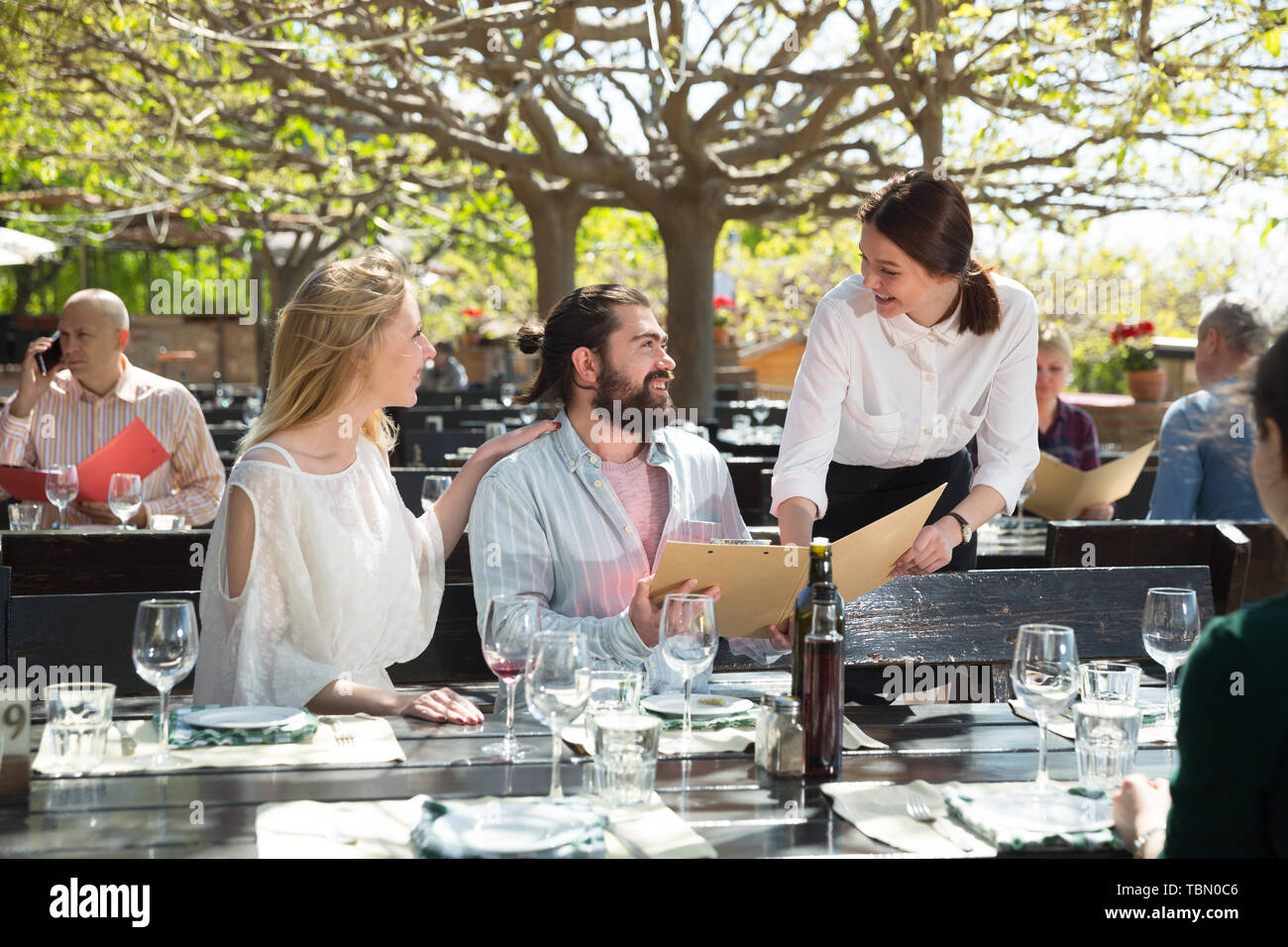Hospitable waitress helping visitors with menu on outdoor terrace of ...