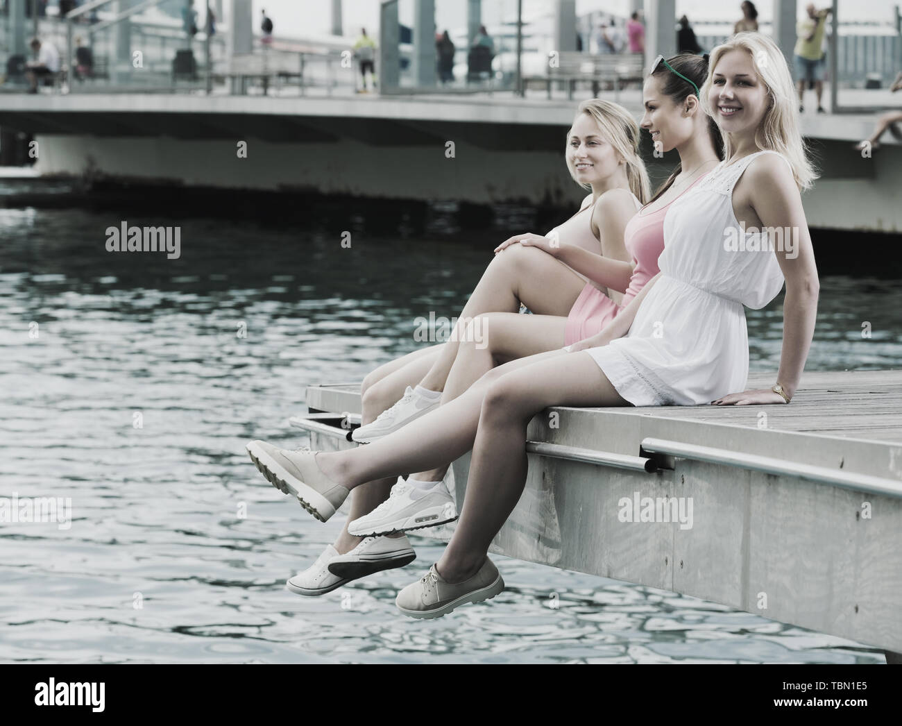 three young women friends sitting on harbour sidewalk in town on summer ... three young women friends sitting on harbour sidewalk in town on summer ...