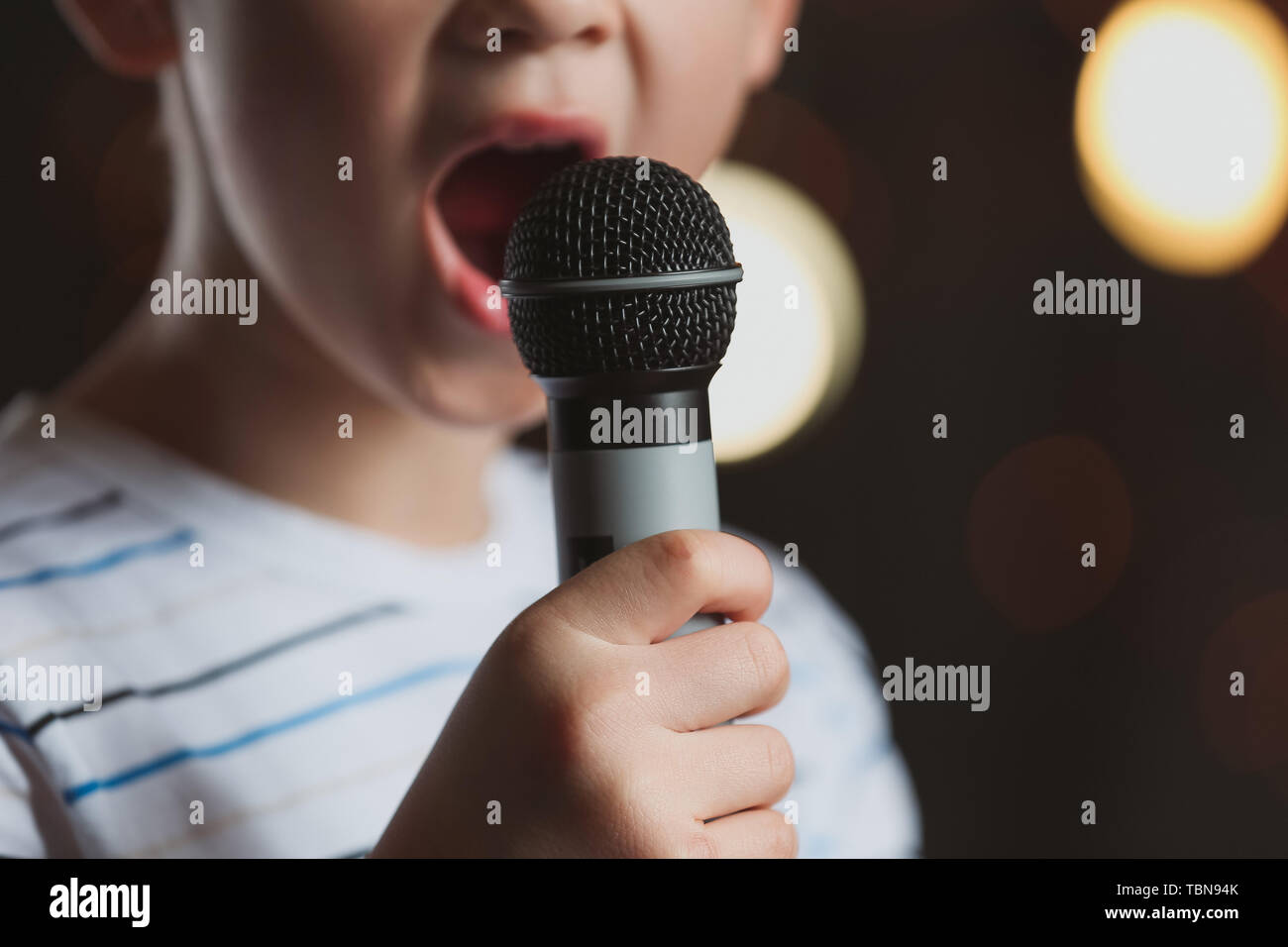Cute little boy with microphone singing against dark background ...