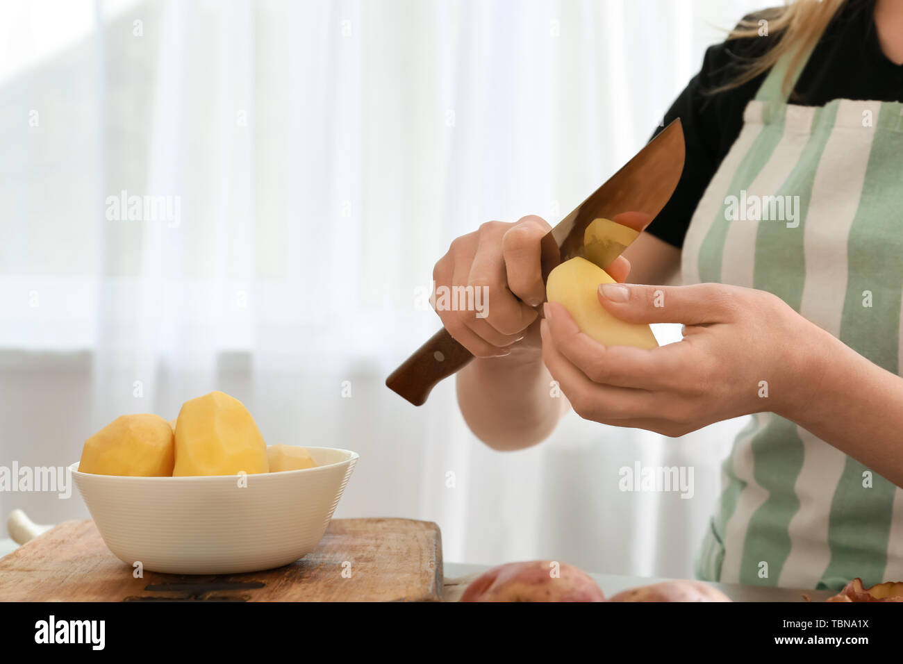 Woman peeling raw potato at table in kitchen Stock Photo - Alamy