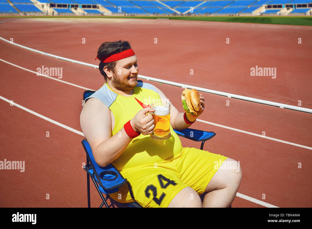 Fat man eating a burger and beer while sitting in training at the ...
