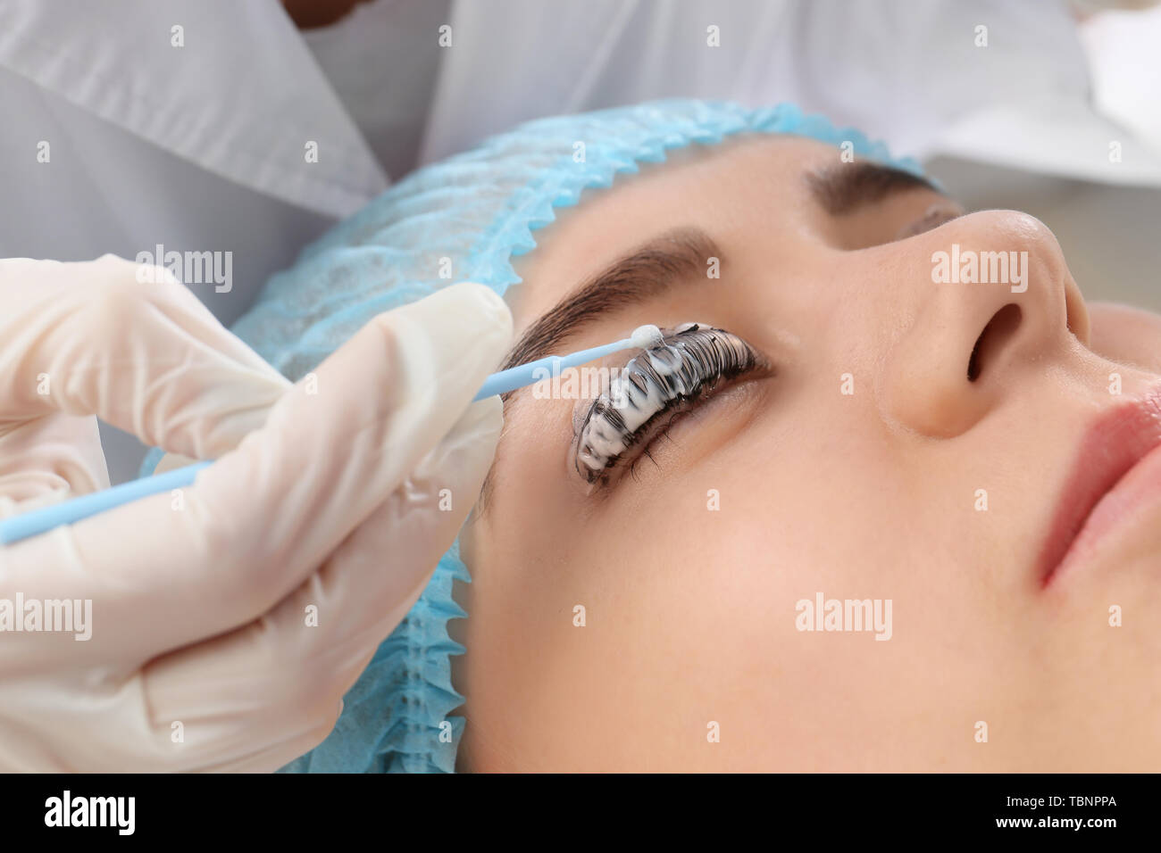Young woman undergoing procedure of eyelashes dyeing and lamination in ...