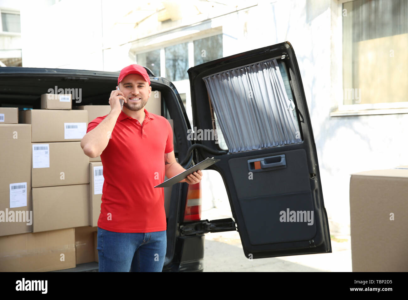 Delivery man talking by phone while standing near car with parcels ...