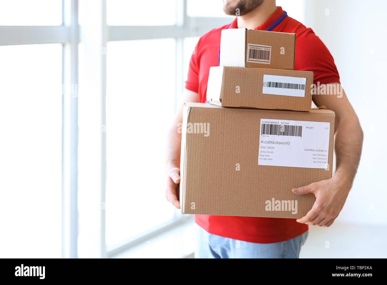 Handsome delivery man with boxes indoors Stock Photo - Alamy
