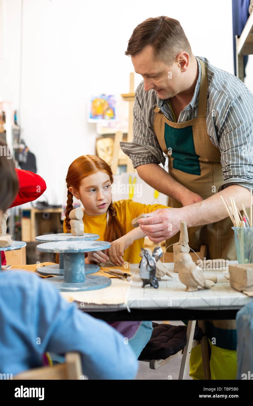 Standing near pupil. Male art teacher wearing apron standing near his ...