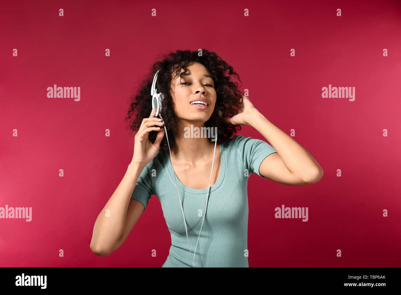 Young African-American woman listening to music on color background ...