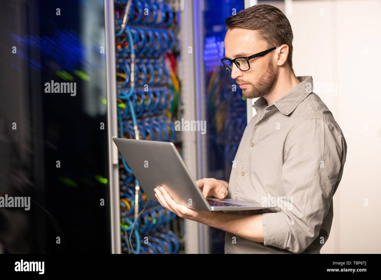 Serious thoughtful handsome young server engineer in glasses standing ...