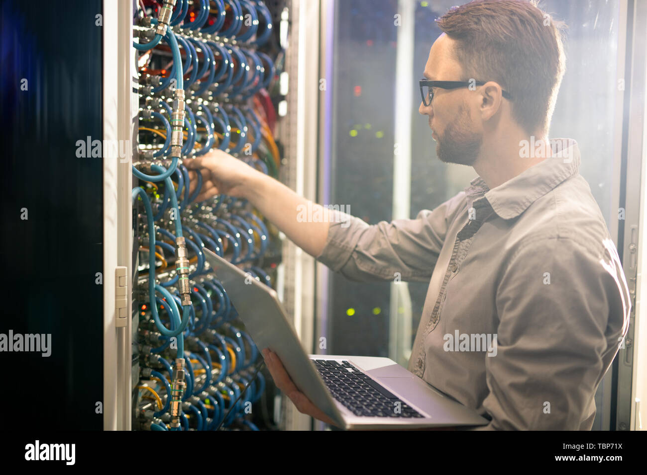 Serious busy young male engineer in glasses standing against mainframe ...