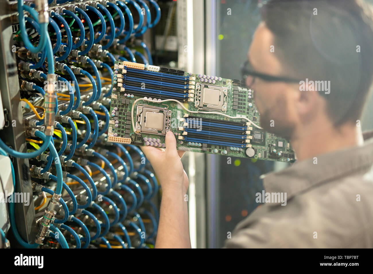 Busy skilled young IT expert in glasses standing by server cabinet and ...