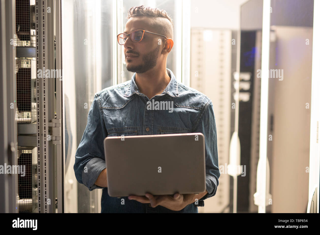 Serious confident young Arabian IT engineer with beard standing in data ...