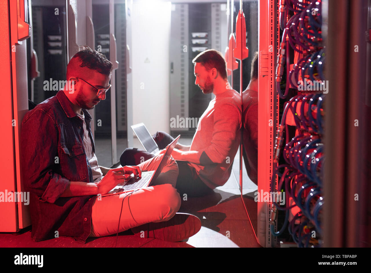 Serious busy multi-ethnic IT engineers sitting on floor in server ...