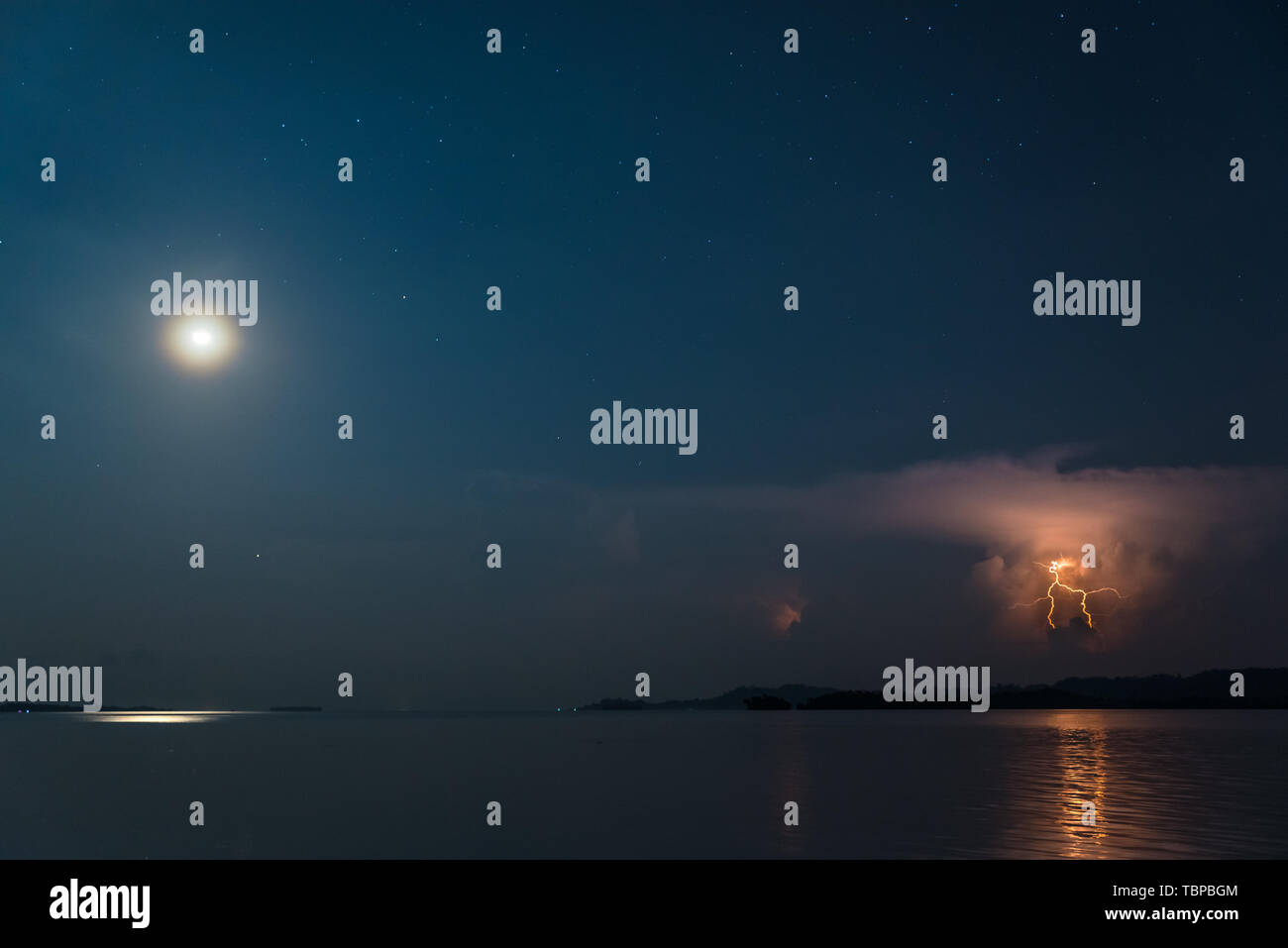 Lightning in the night starry sky with moon reflection over water ...