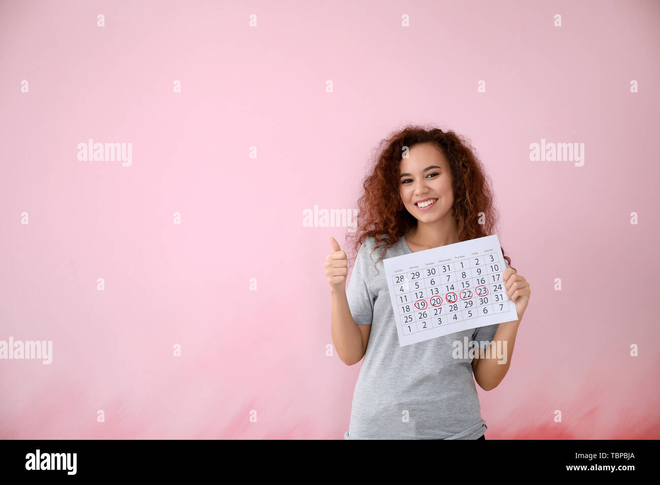 African-American woman holding calendar with marked days of ...