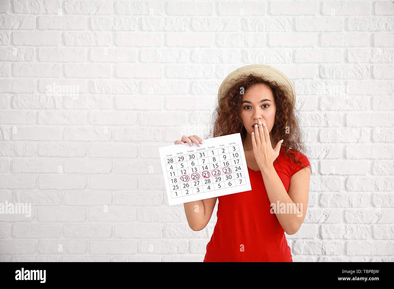 Surprised African-American woman holding calendar with marked days of ...