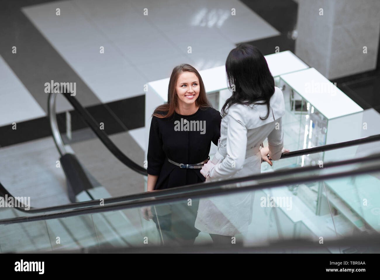 two smiling business women standing on an escalator in a business ...