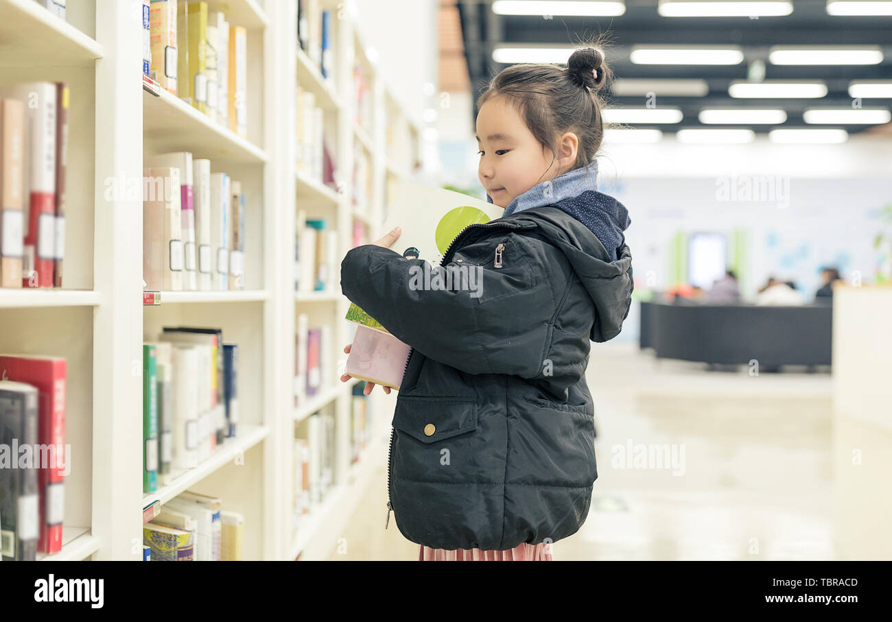 Little Asian girl reading in the library Stock Photo - Alamy