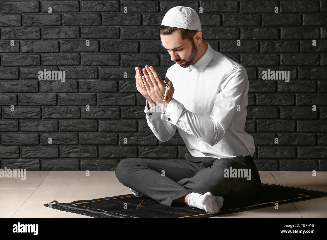 Young Muslim man praying against dark brick wall Stock Photo - Alamy