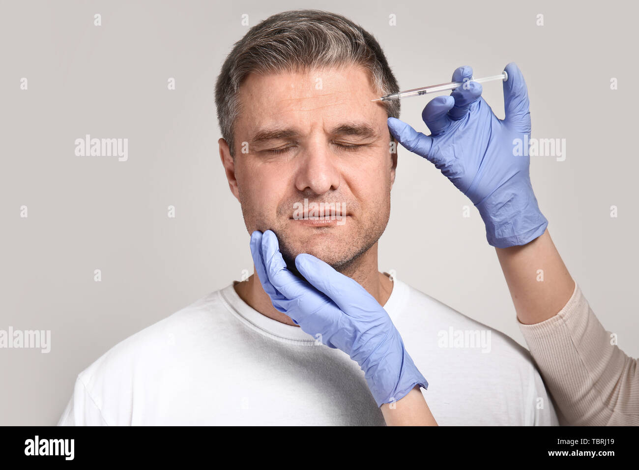 Mature man and hands holding syringe for anti-aging injections on grey ...