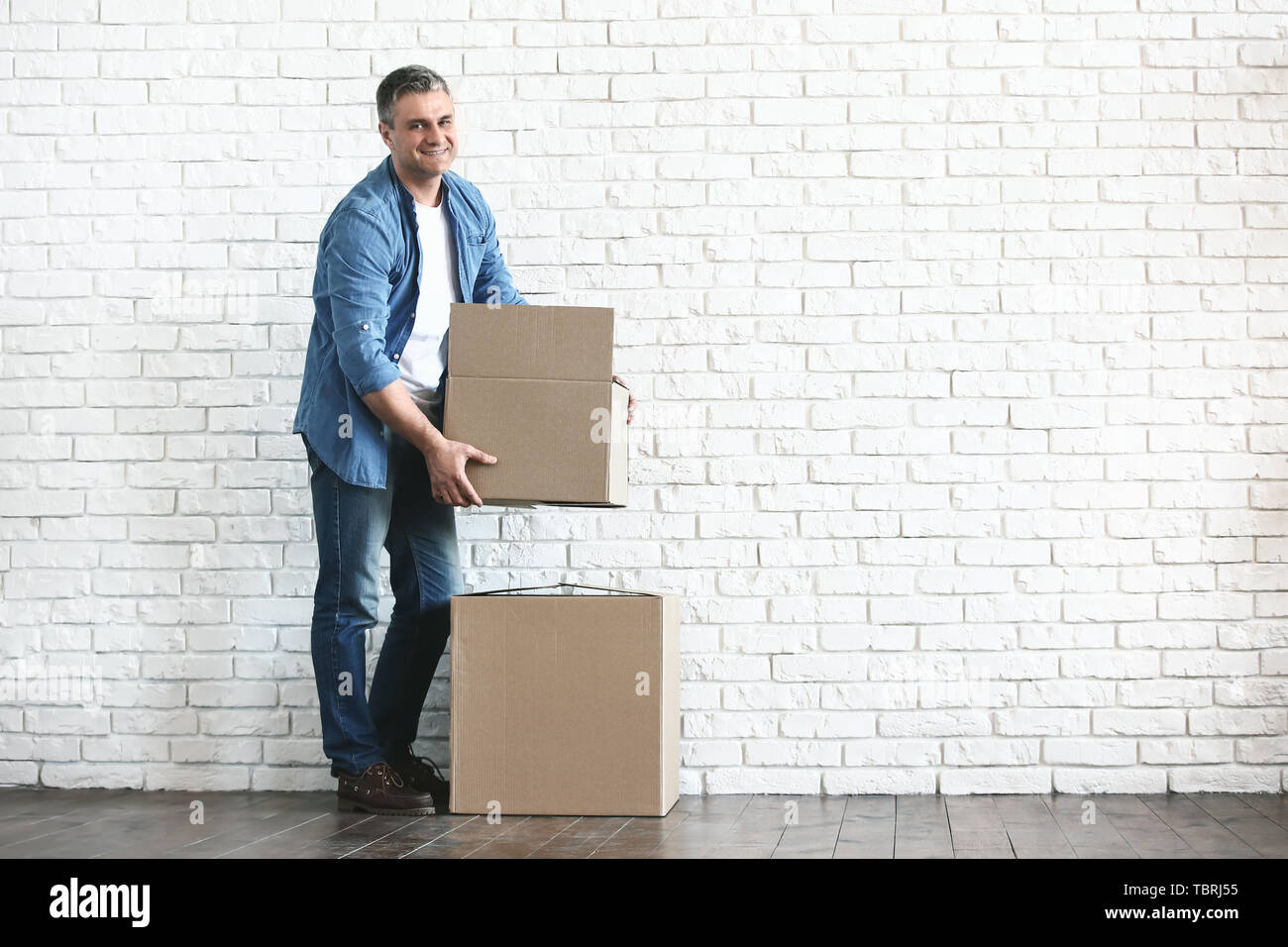 Handsome mature man with moving boxes near white brick wall Stock Photo ...