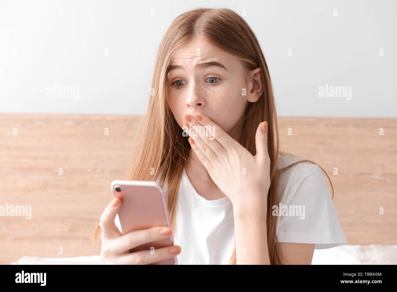 Afraid teenage girl with mobile phone in bedroom at home Stock Photo ...