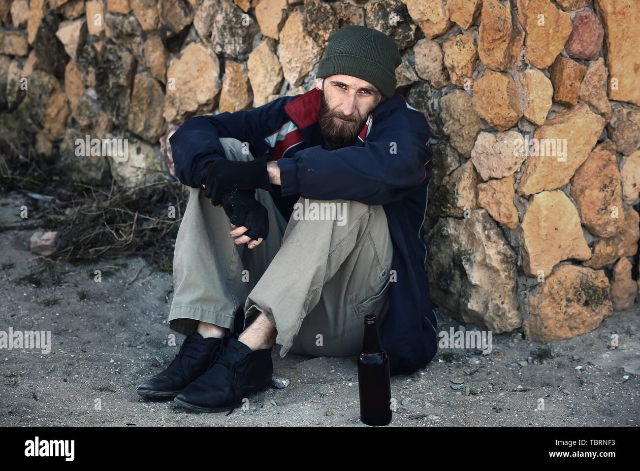 Poor homeless man sitting near wall outdoors Stock Photo - Alamy